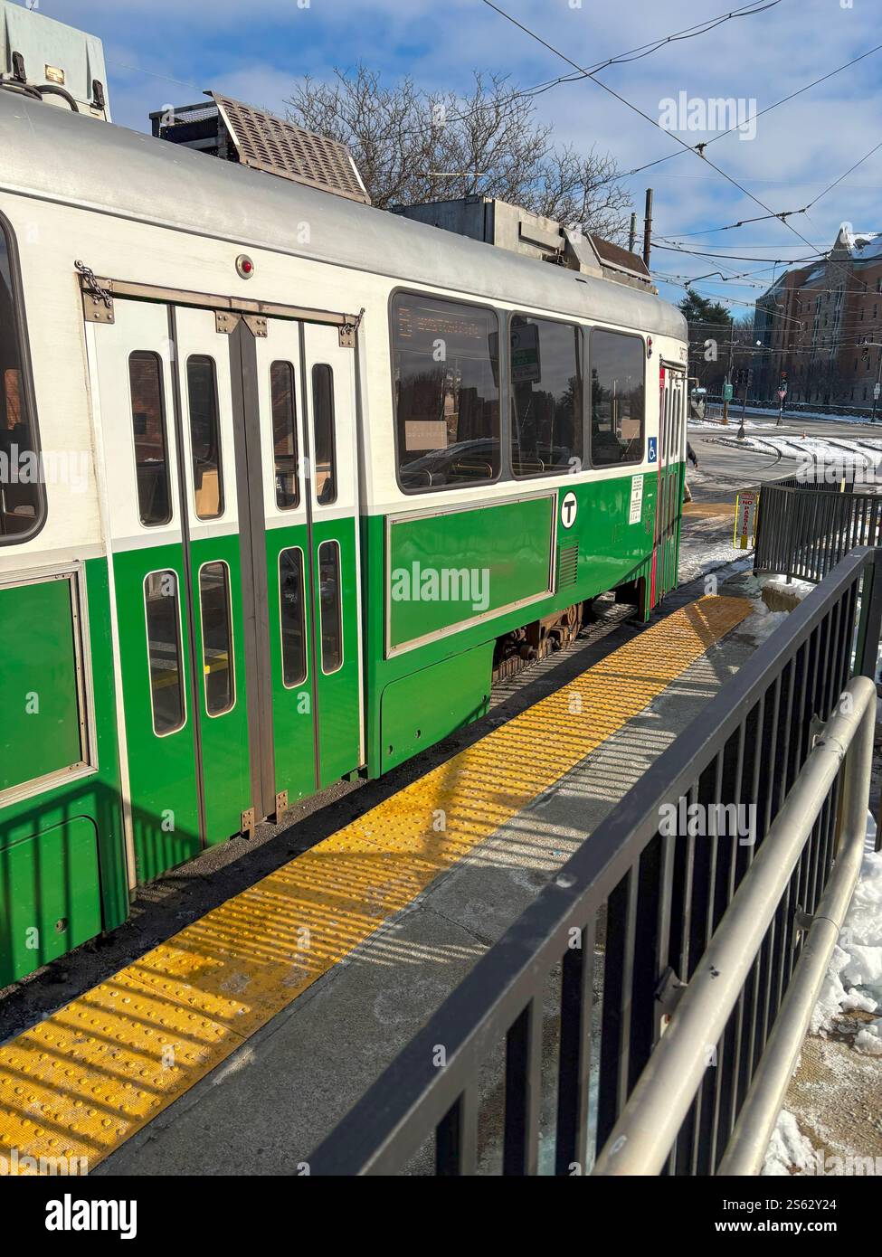 A green train is waiting at a bustling urban station under a clear blue ...