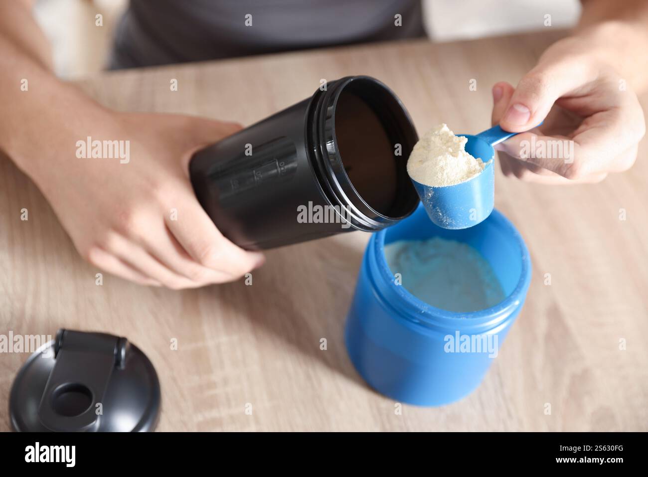 Making protein cocktail. Man adding powder into shaker at wooden table ...