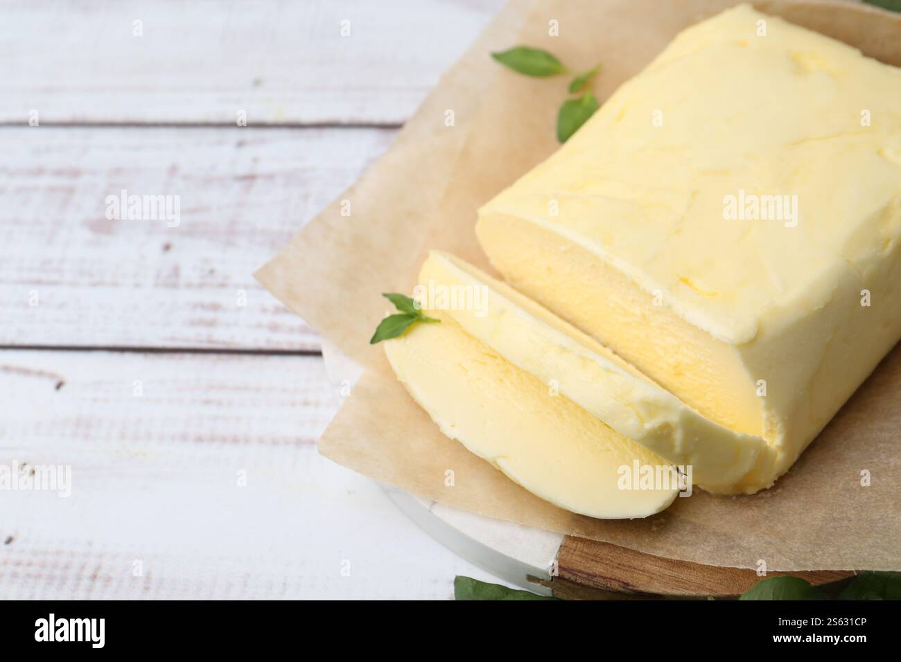Cut brick of butter and basil on white wooden table, closeup. Space for ...