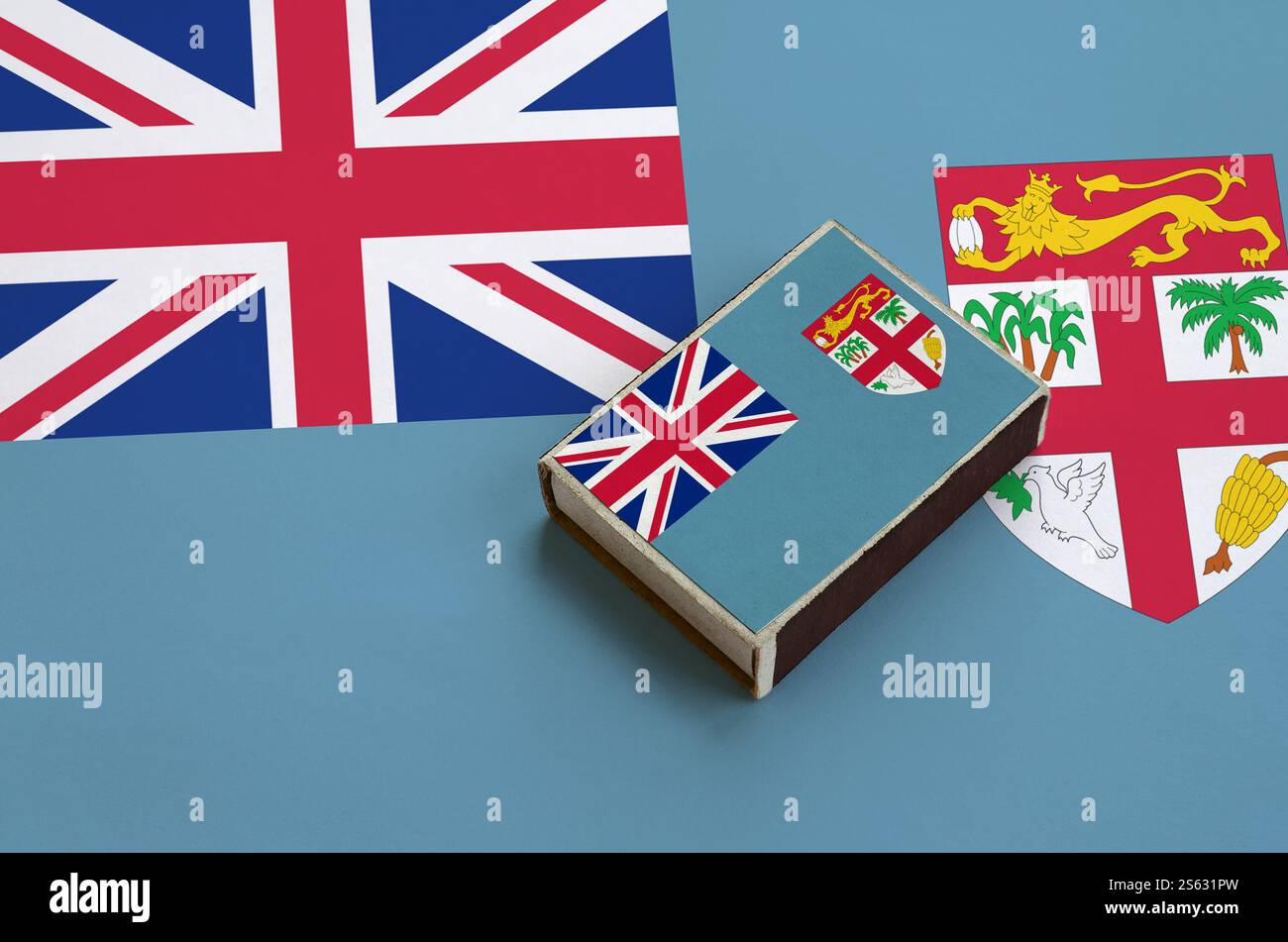 Fiji flag is pictured on a matchbox that lies on a large flag. Fiji ...