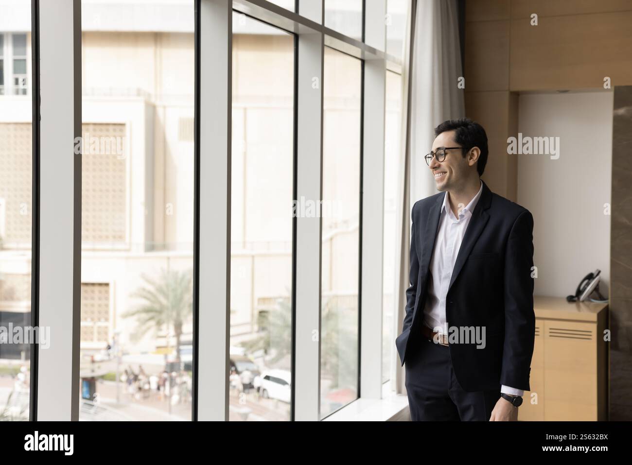 Happy Arabian company boss looks out window with positive expression ...