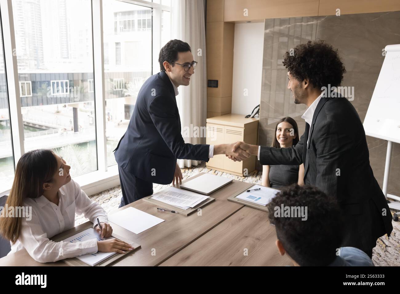 Young Arabian businessmen in suits shake hands over conference table ...