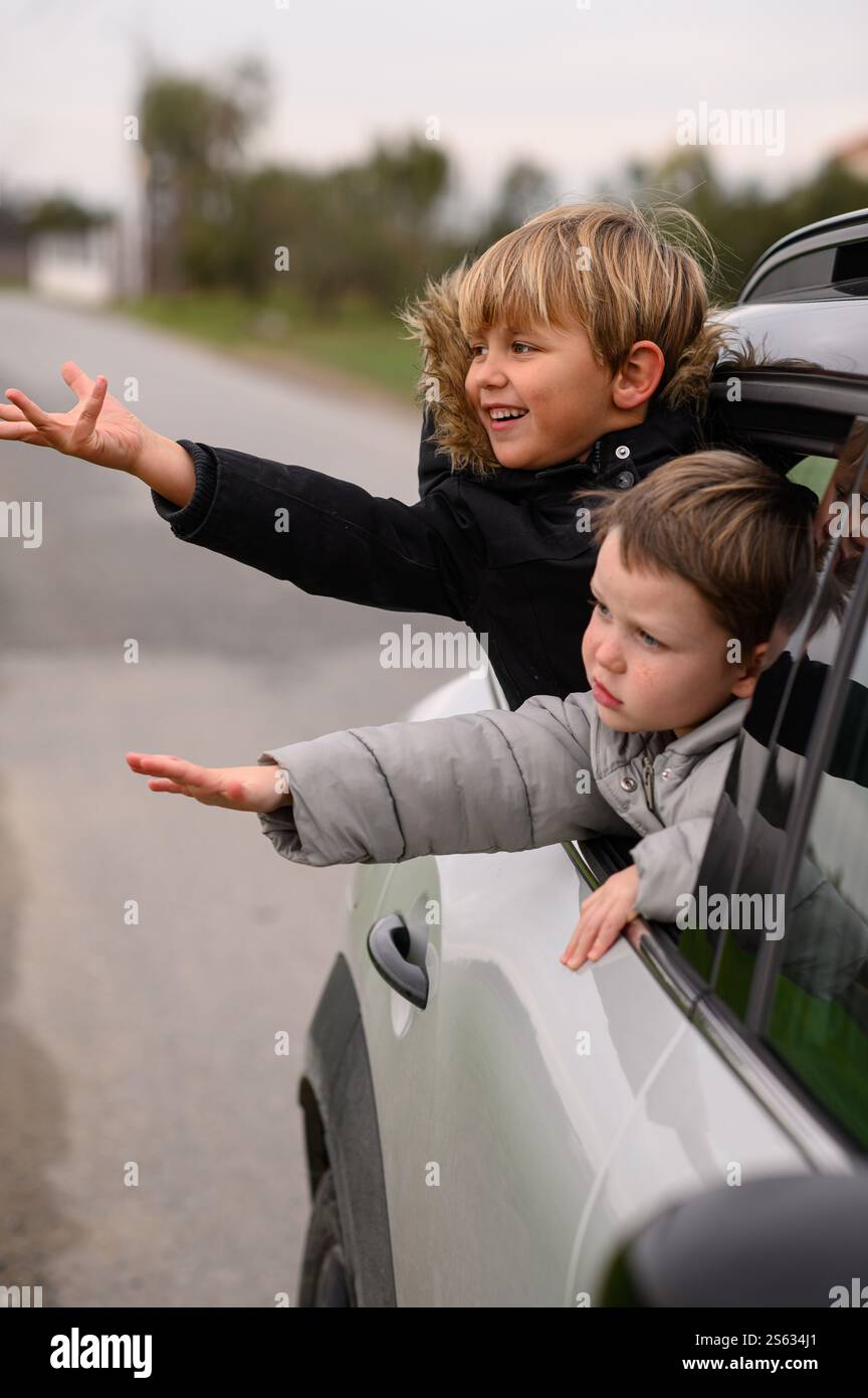 Boys lean out of a moving car’s windows, laughing and enjoying the ...
