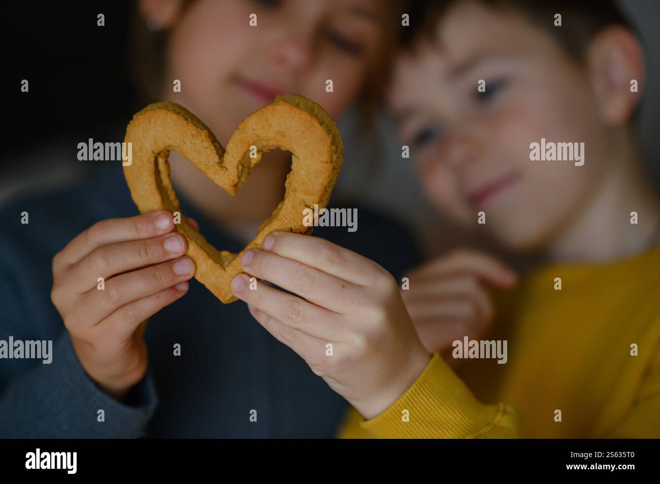 A boy and a girl are playfully biting a heart-shaped cookie from ...