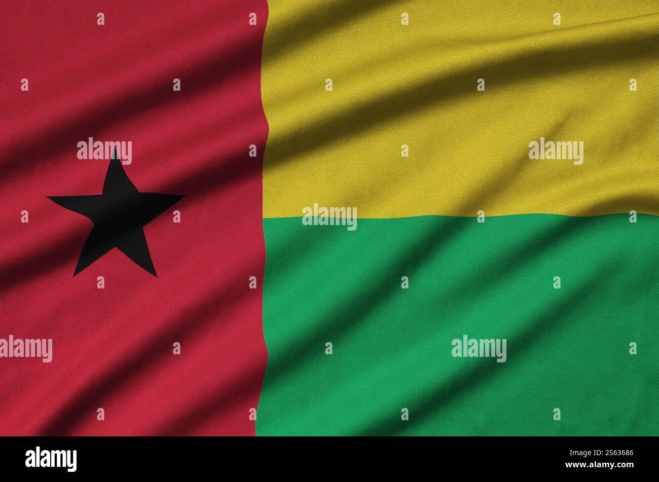 Guinea Bissau flag is depicted on a sports cloth fabric with many folds ...