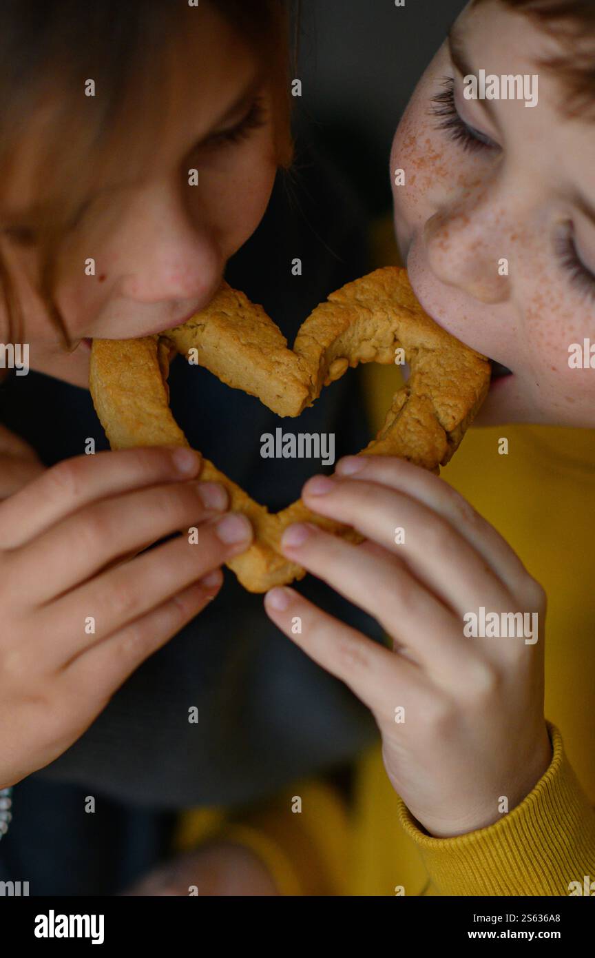 A boy and a girl are playfully biting a heart-shaped cookie from ...