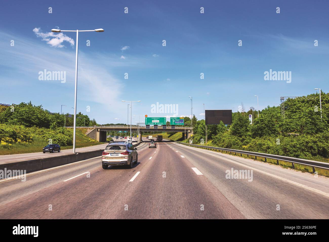 Cars driving on highway under clear blue sky with road signs and bridge ...