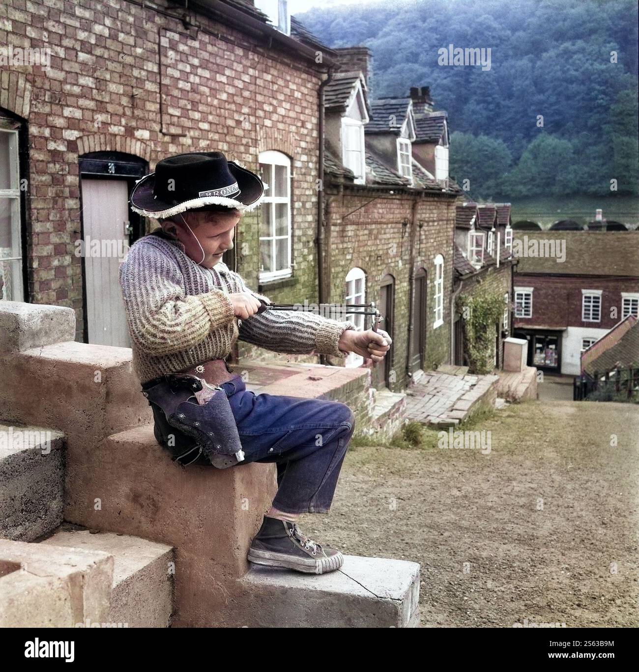 Young boy playing alone with a catapult and wearing a cowboy outfit ...