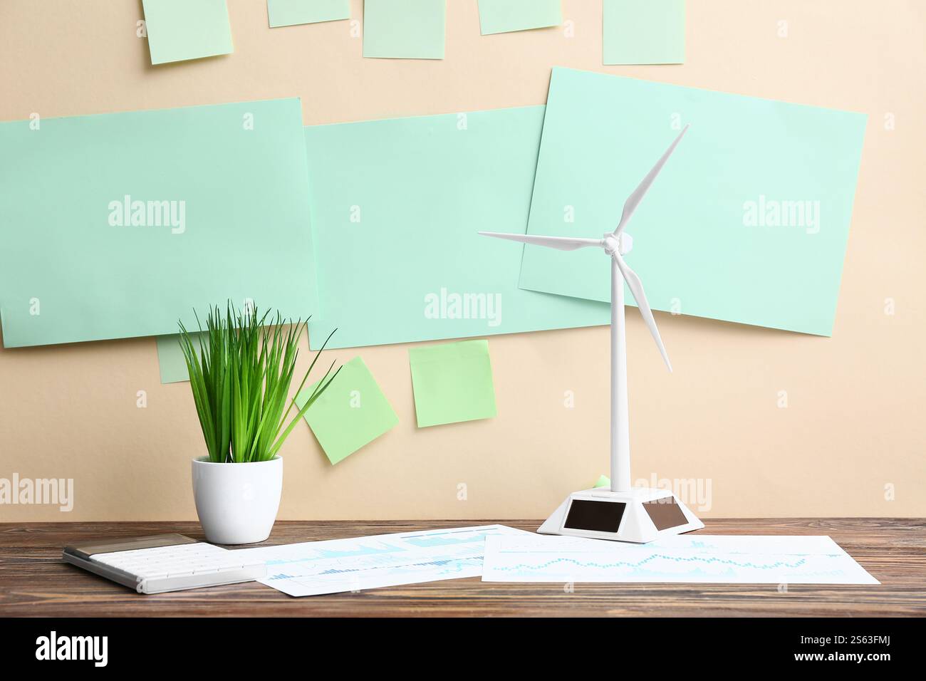 Blank papers and wind turbine model with diagrams on table near beige ...