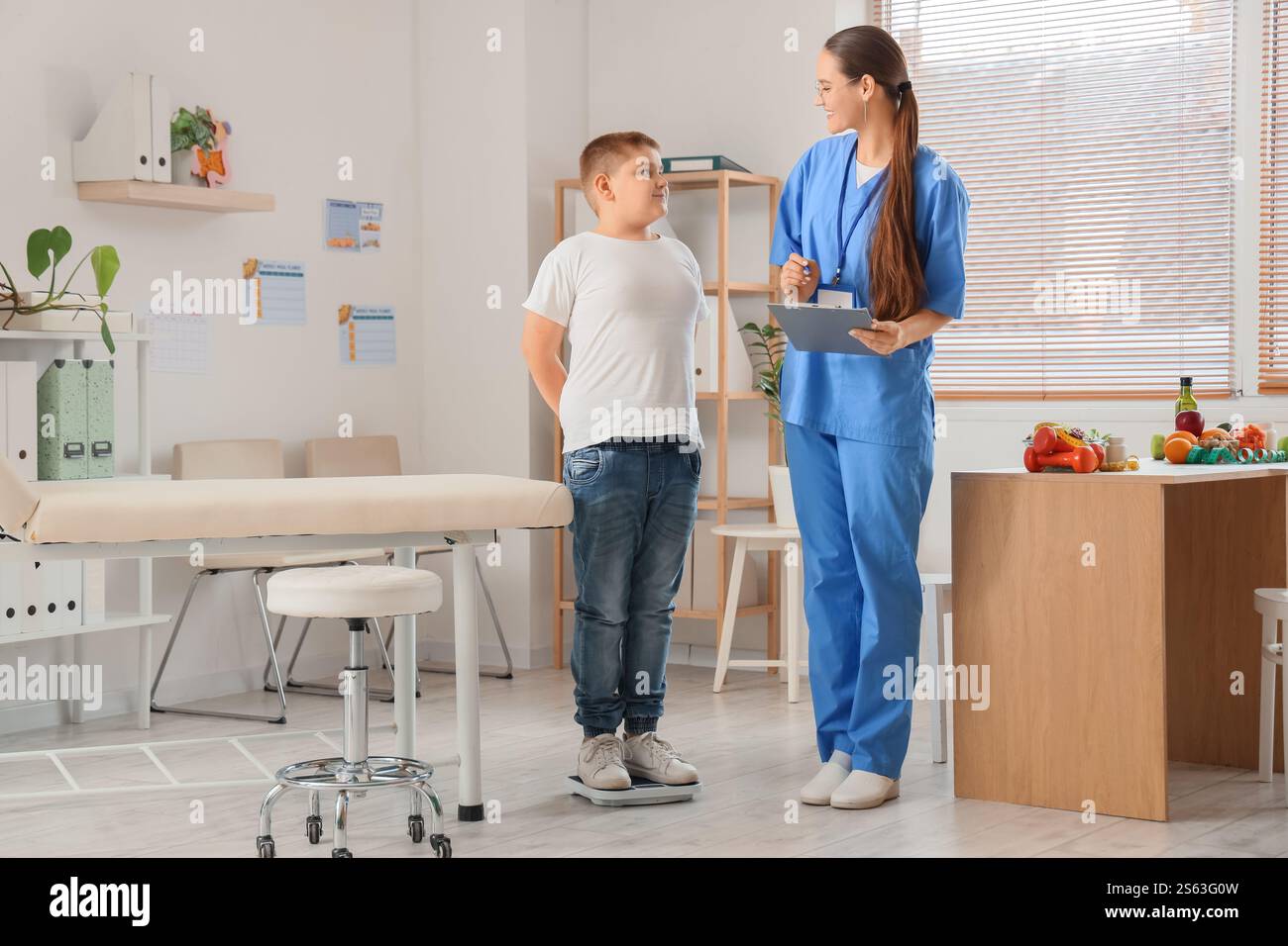 Overweight boy with nutritionist measuring weight on scales in clinic ...