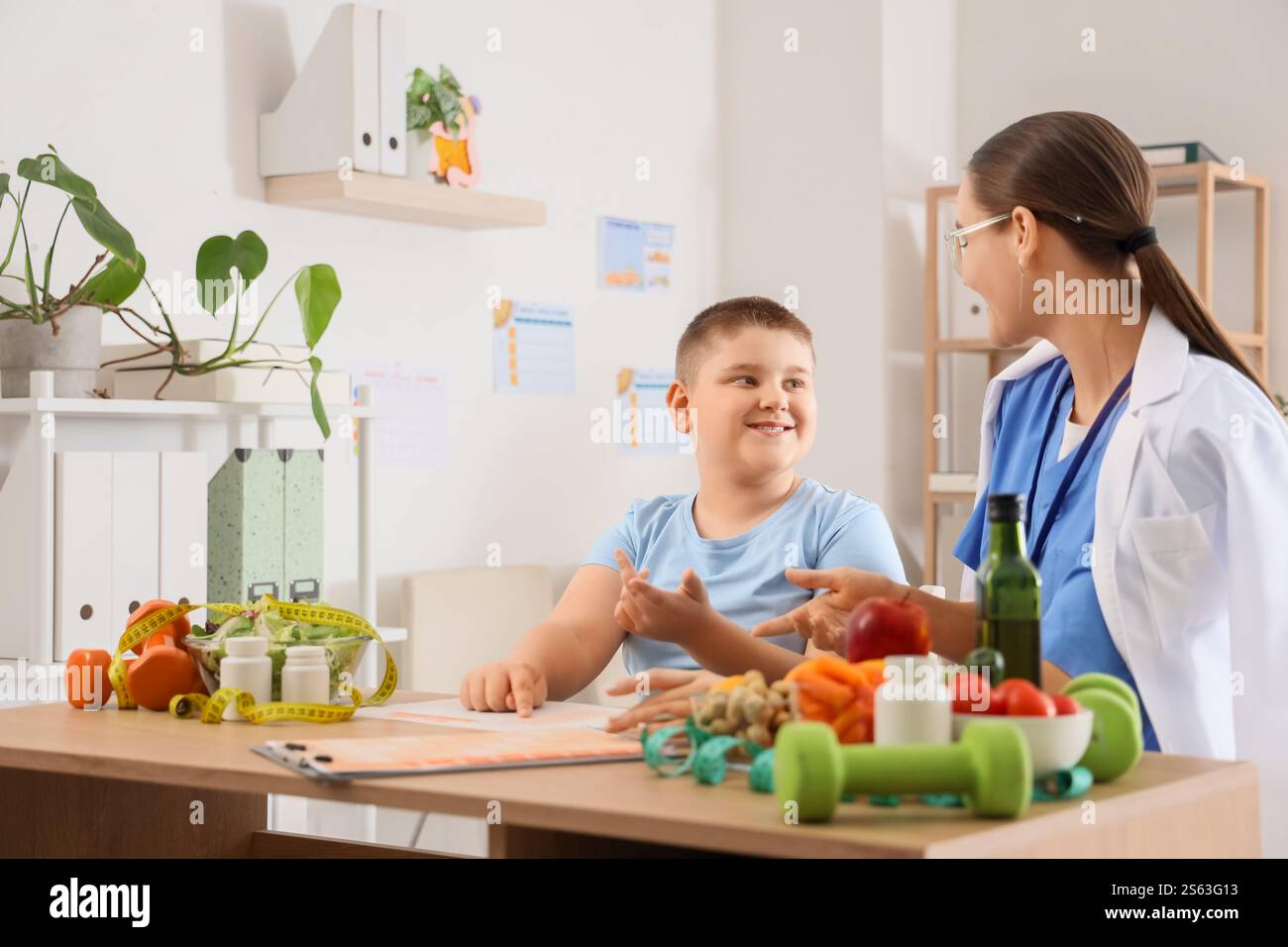 Overweight boy with nutritionist making meal plan at table in clinic ...