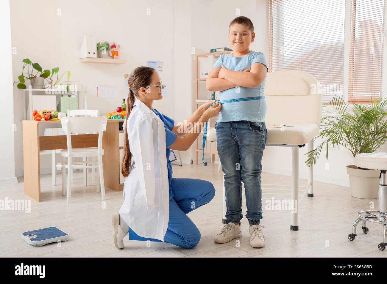 Female nutritionist measuring overweight boy's belly on scales in ...