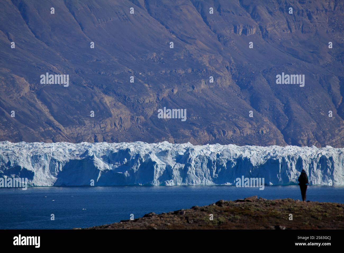 A visitor at Karrat Island with a huge iceberg floating in Karrat Fjord ...
