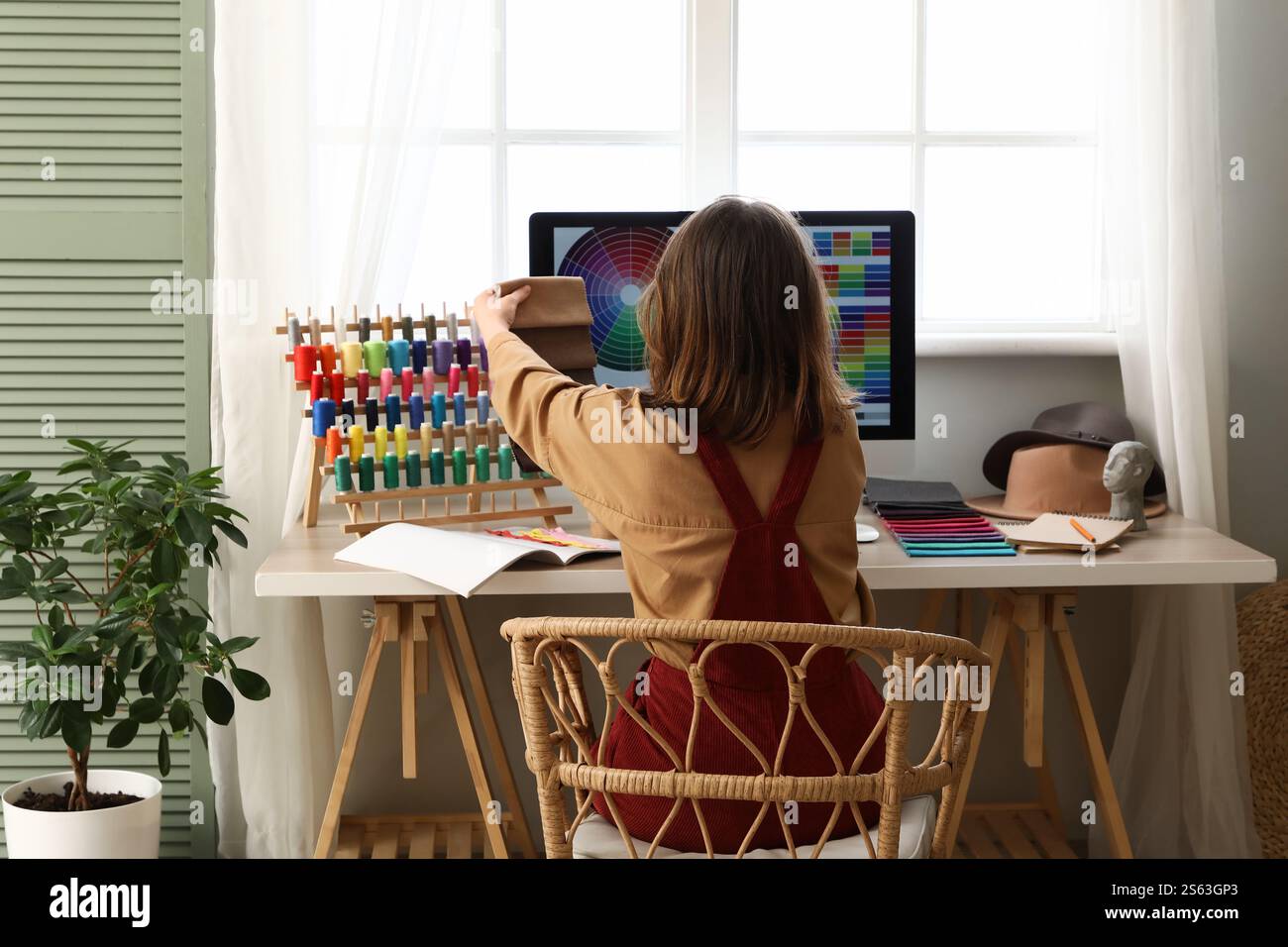 Female tailor working with computer and thread spools at table in ...