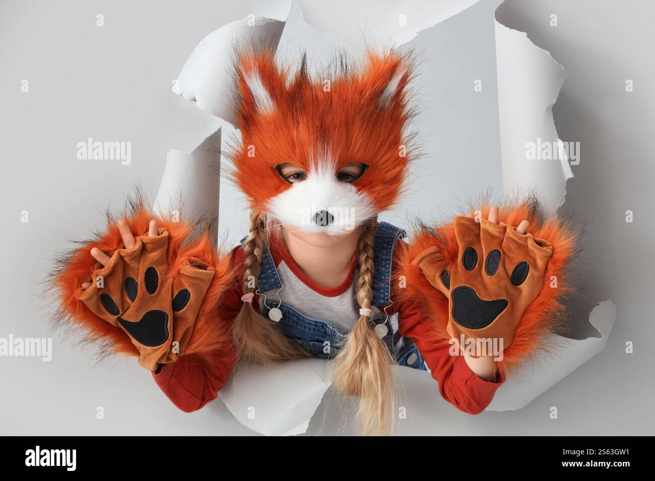 Quadrober girl in fox mask visible through torn paper on light ...