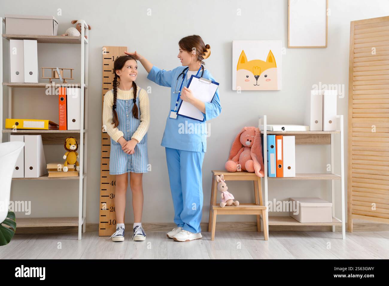 Female pediatrician measuring height of cute girl near stadiometer in ...