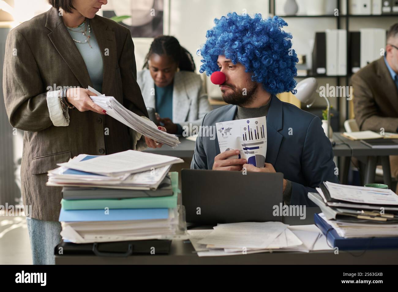 Young businessman in clown wig and nose looking at stack of paper ...