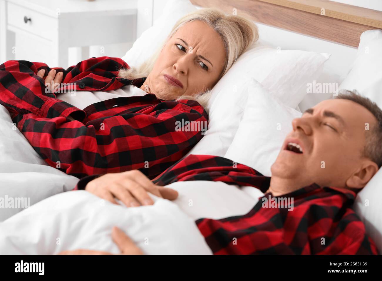 Displeased mature woman lying with her snoring husband in bedroom Stock ...