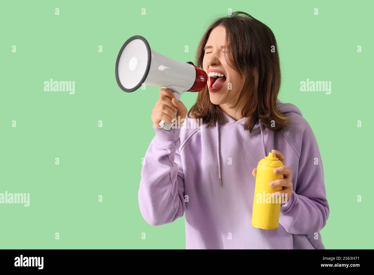 Young woman with paint spray can shouting into megaphone on green ...