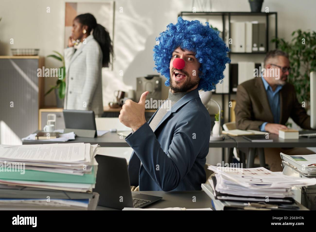 Young cheerful male manager in formalwear, clown wig and nose looking ...