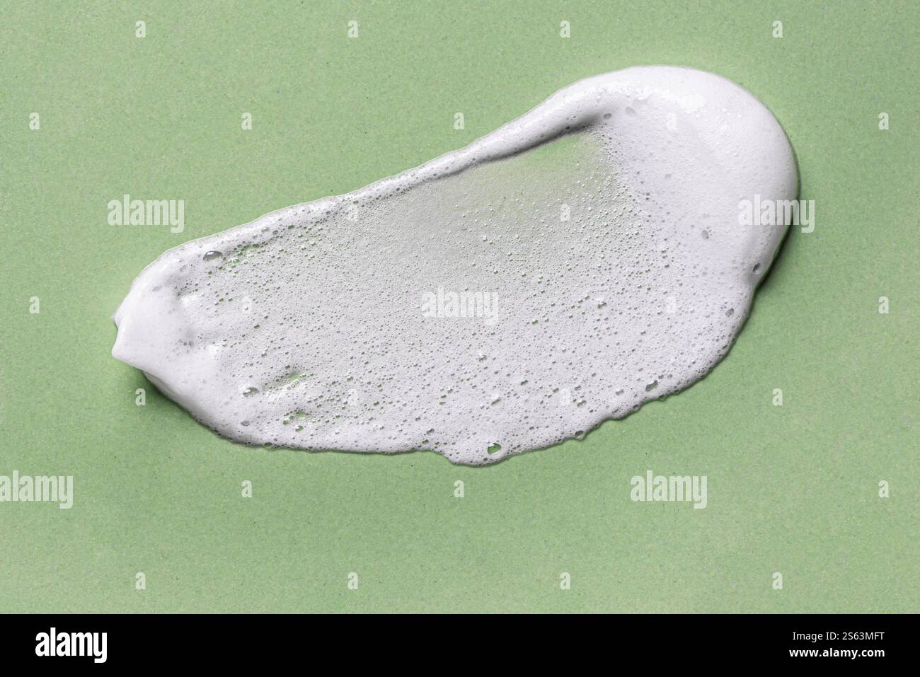 White face cleanser mousse texture swatch on olive green background ...