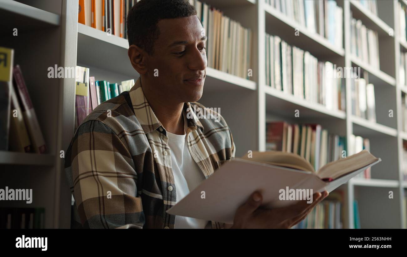 African American man sitting library floor bookcase reading book ...