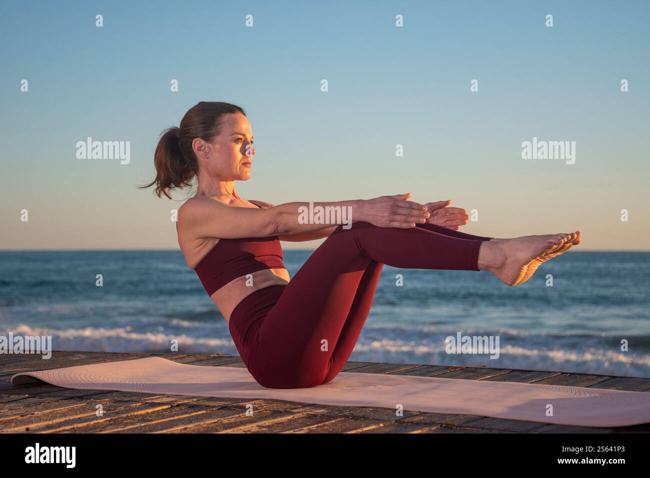 sporty woman doing boat pose outdoors by the ocean, core muscle workout ...