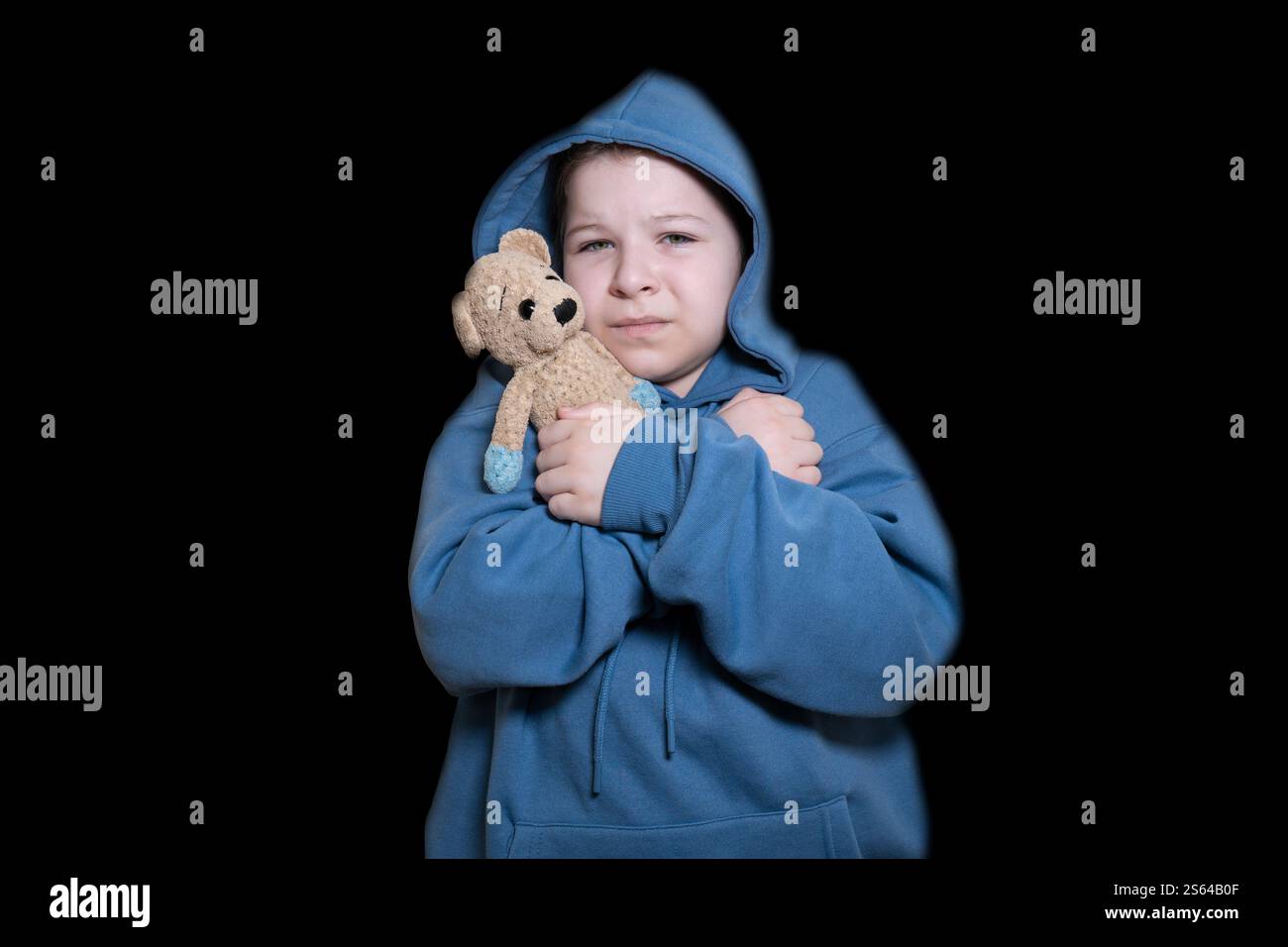A girl wearing a blue hoodie in the dark hugging a teddy bear. Concept ...