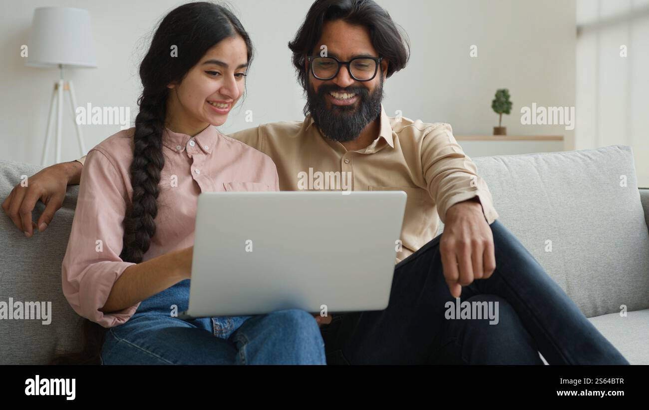 Arabian Indian couple on couch sofa use computer laptop shopping online ...