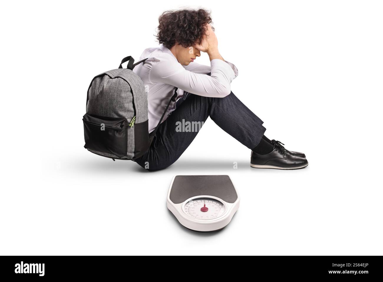 Worried male student siting on the floor next to a weight scale ...