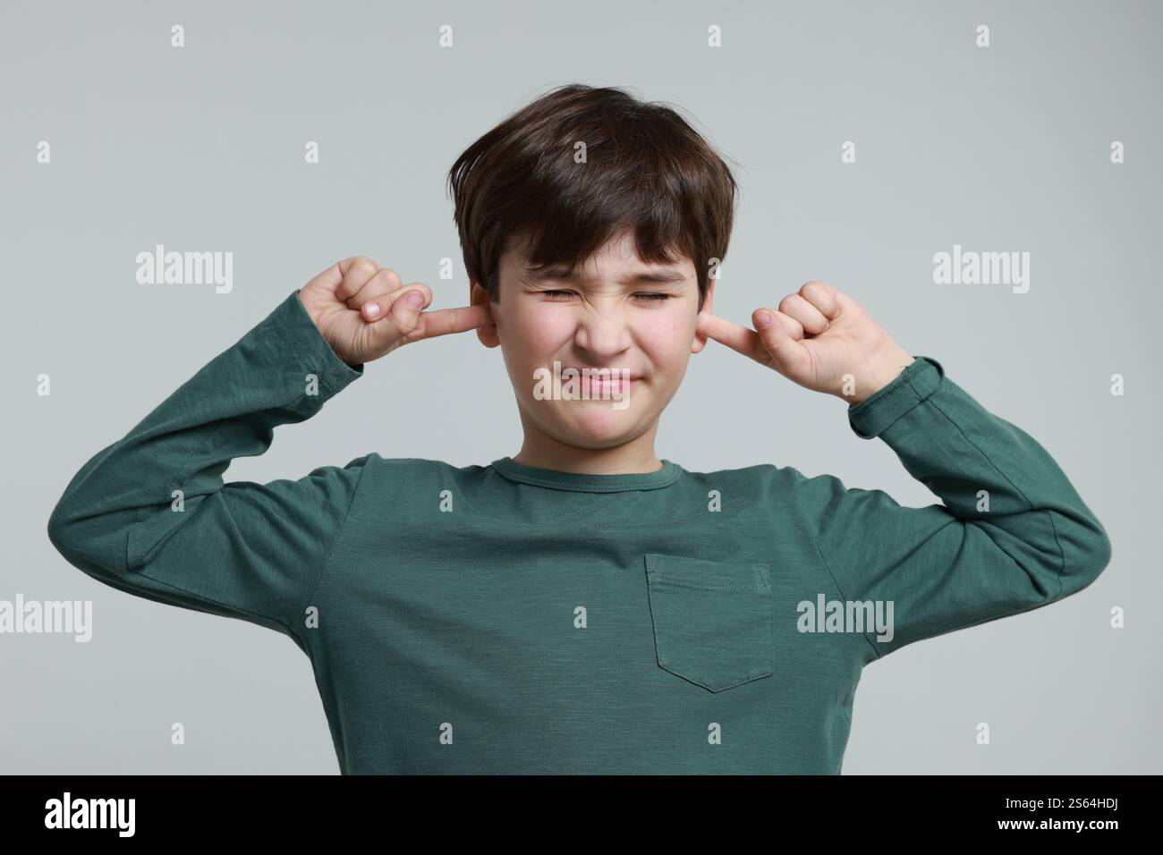Annoyed boy covering his ears due to loud sound on grey background ...