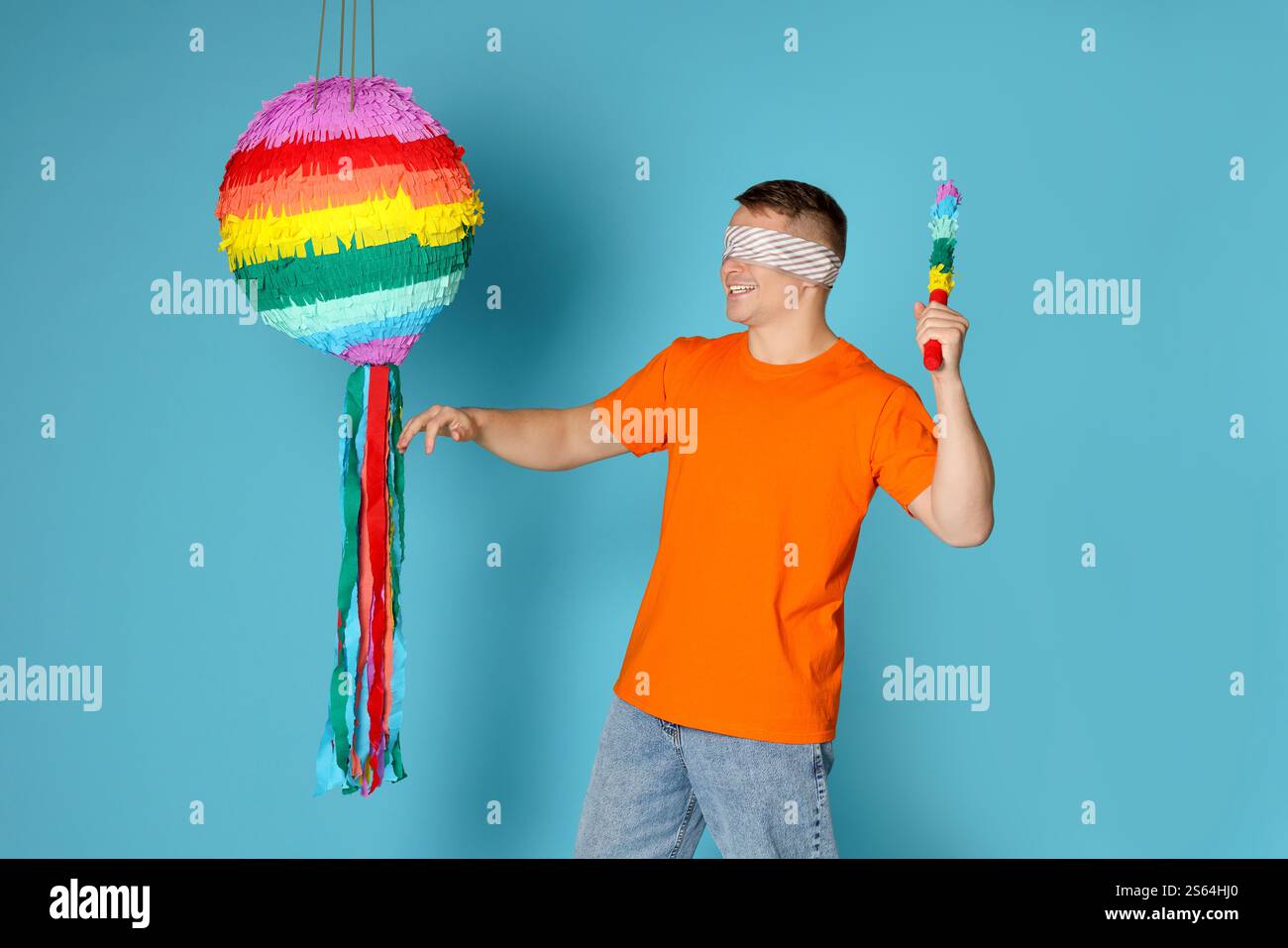 Man with tied eyes breaking pinata on light blue background Stock Photo ...