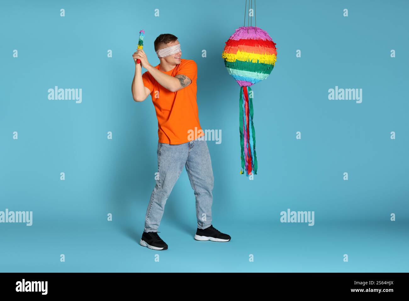 Man with tied eyes breaking pinata on light blue background Stock Photo ...