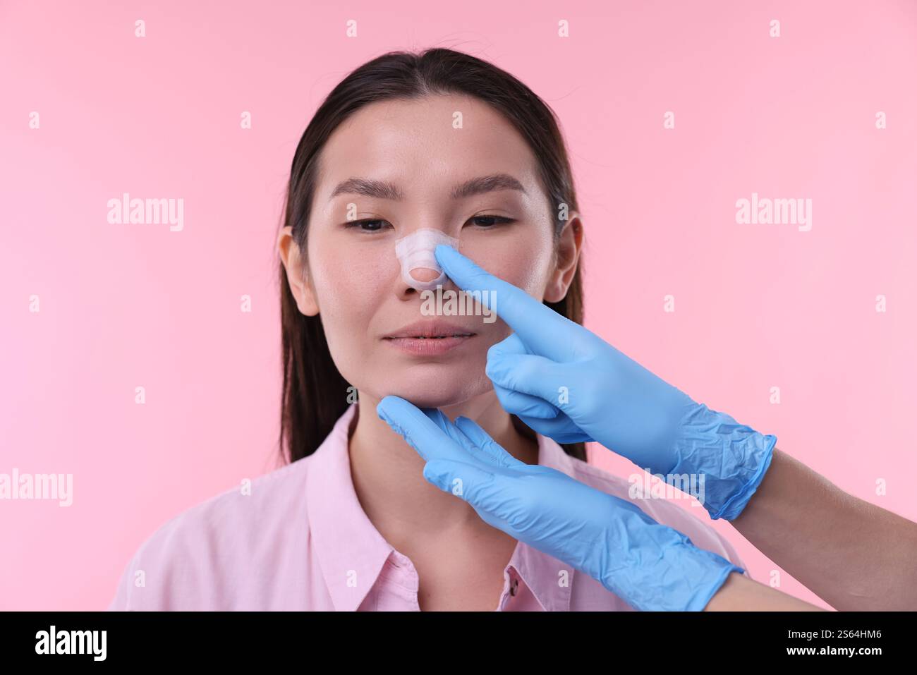 Doctor checking patient's nose after plastic surgery operation on pink ...