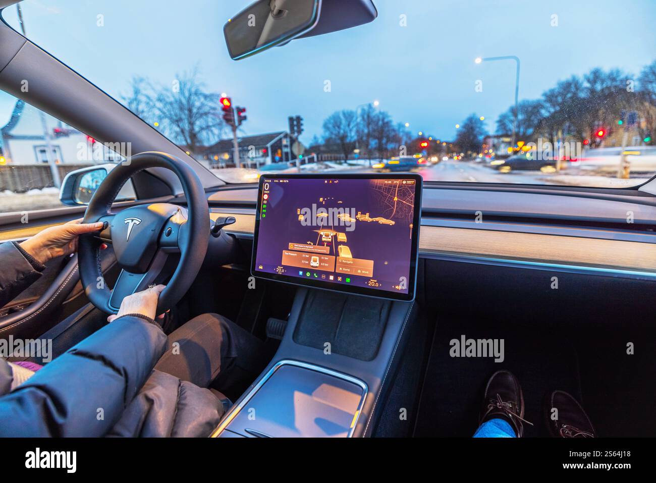 Woman driving Tesla Model Y through city at dusk with navigation and ...