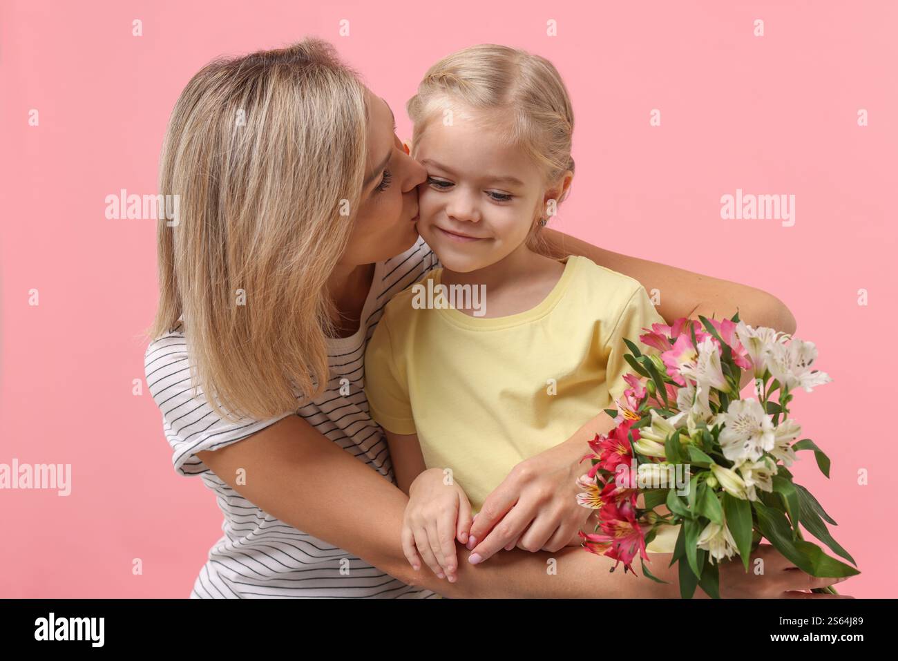 Little daughter congratulating her mom with bouquet of alstroemeria flowers on pink background ...