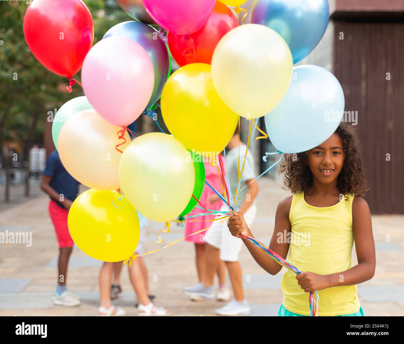 Smiling african american tween girl with balloons on city street Stock ...
