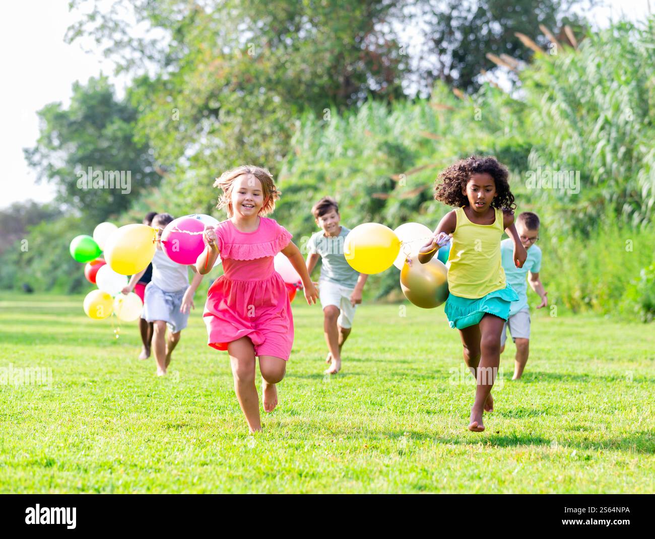 Barefoot children with balloons running through grass Stock Photo - Alamy