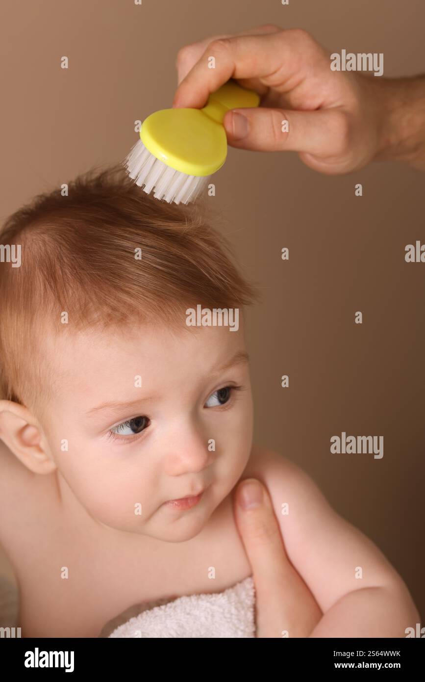 Parents brushing hair of their little baby on dark beige background ...