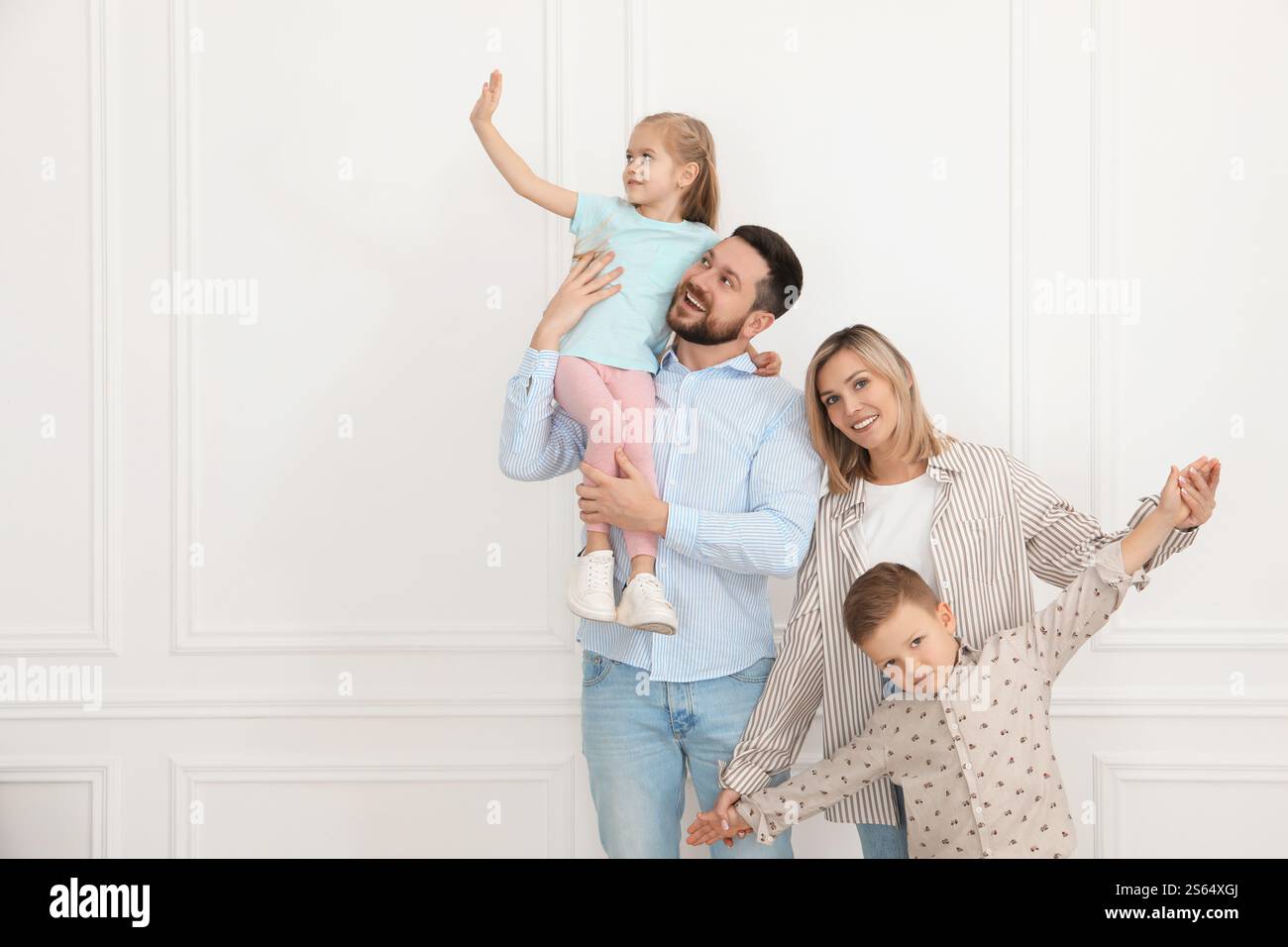 Happy parents and their children near white wall indoors, space for ...