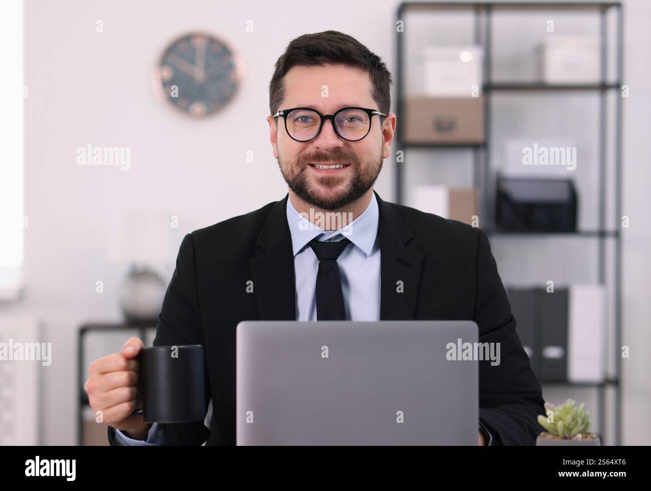 Banker with cup of drink using laptop in office Stock Photo - Alamy
