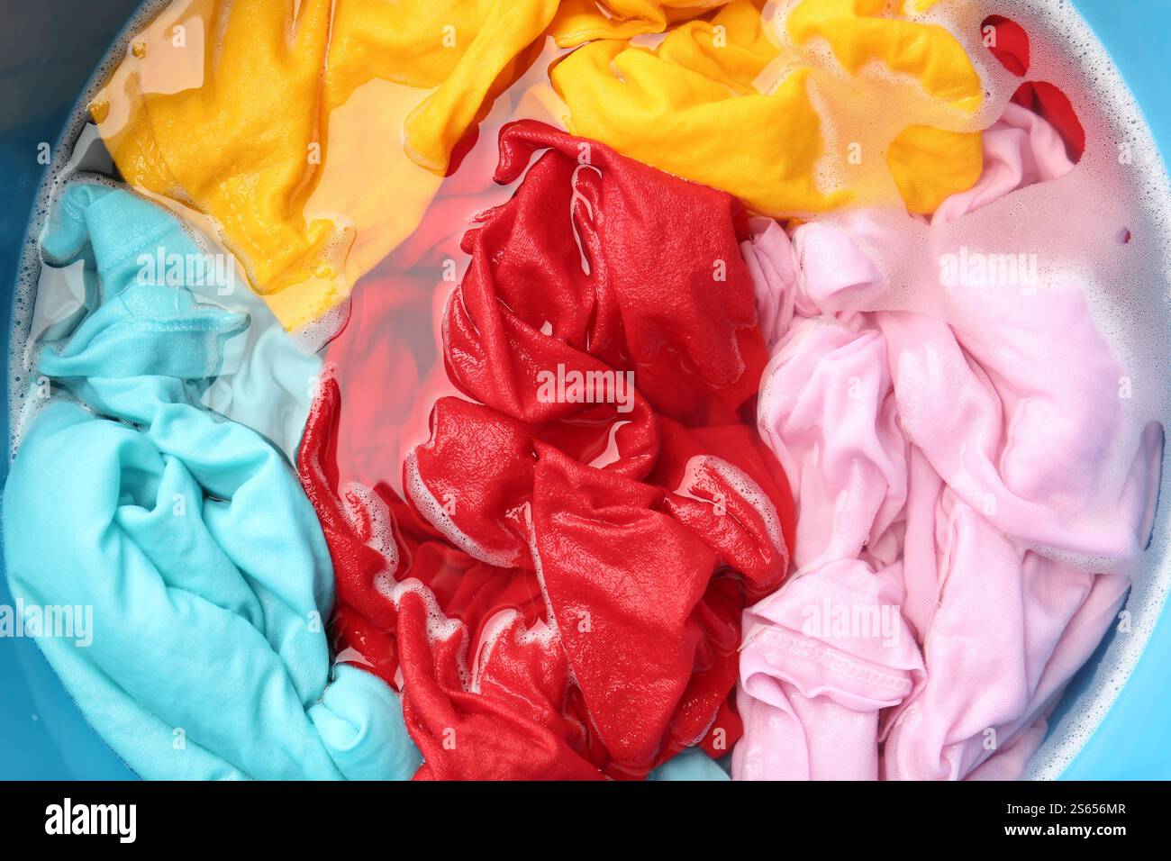 Colorful clothes soaked in water before washing, top view Stock Photo ...