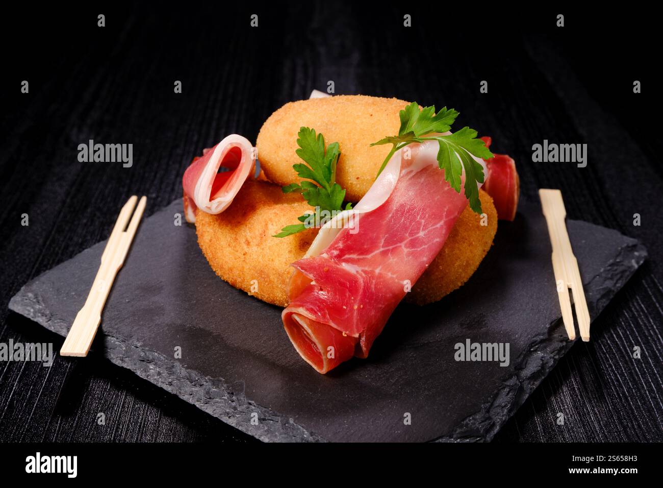 Ham croquettes garnished with cured ham and parsley on a square slate ...