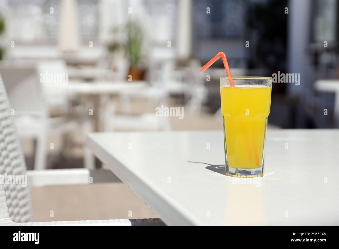 Glass of orange juice with plastic straw on white table in restaurant ...
