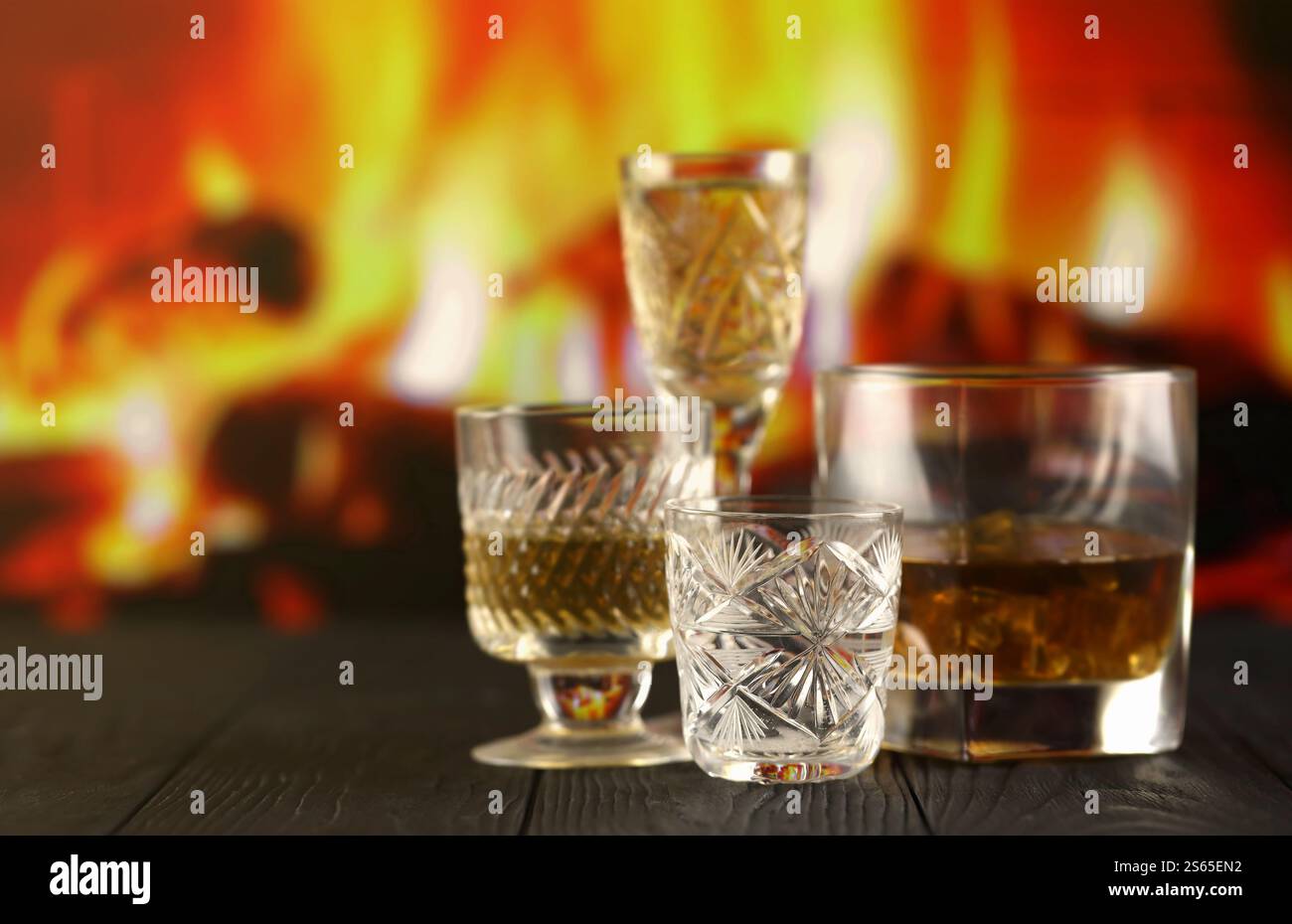 Different alcohol drinks in glass on wooden surface on fireplace ...