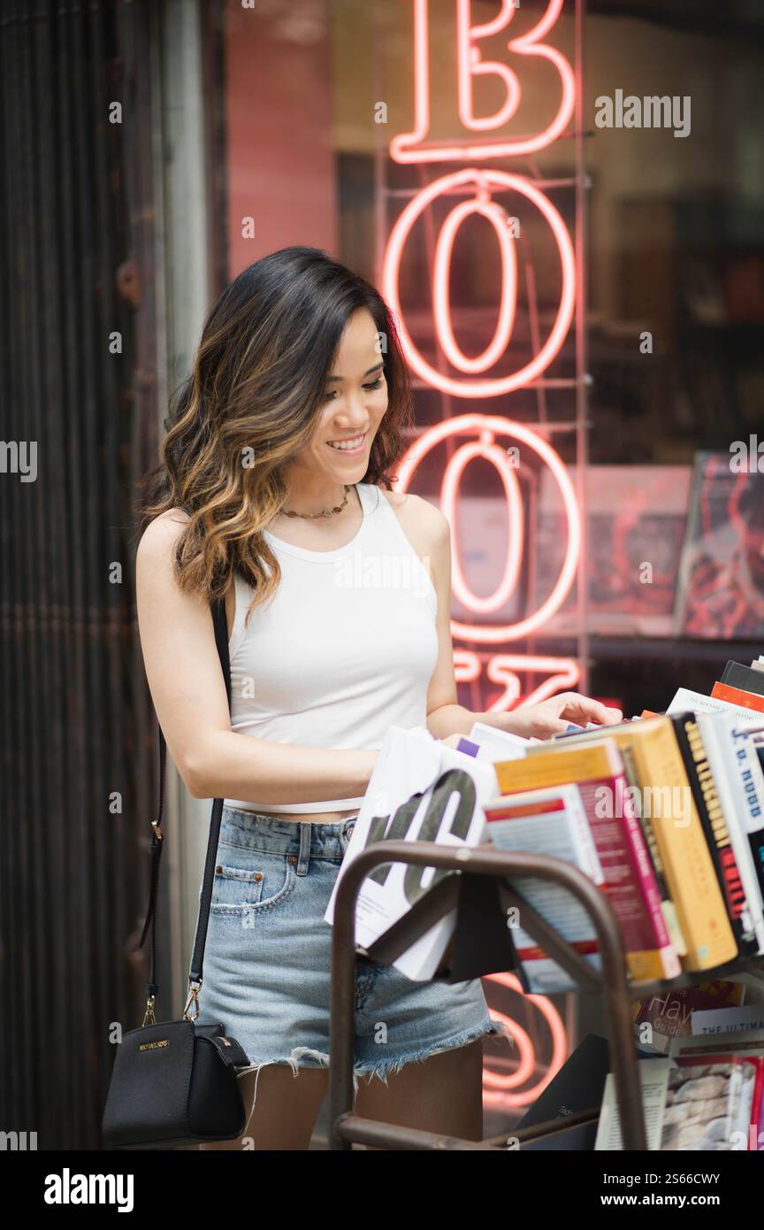 An asian girl is looking through a rack of books outside of a bookstore ...