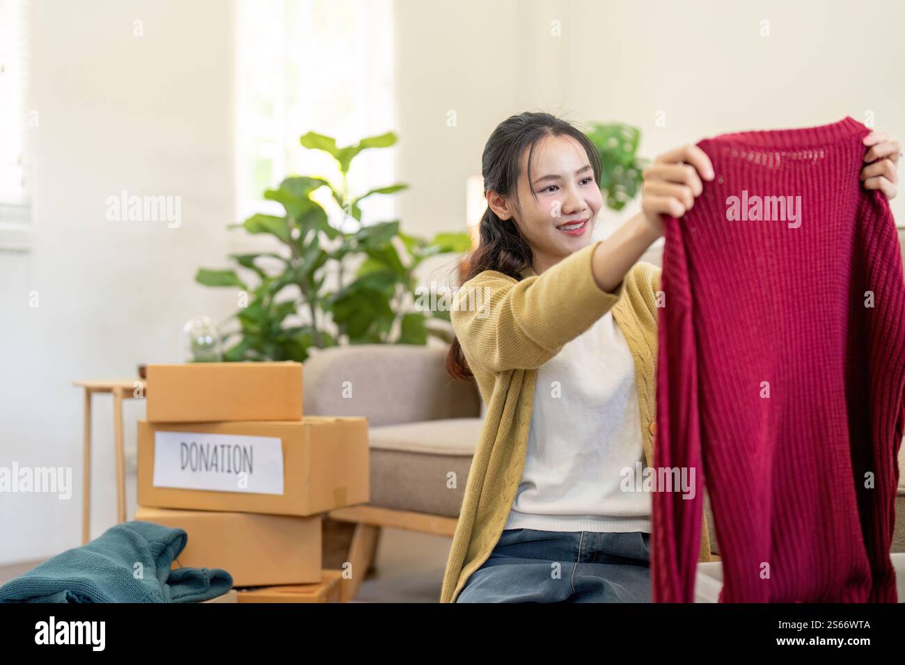 Excited woman showcasing a red sweater for donation in her bright ...