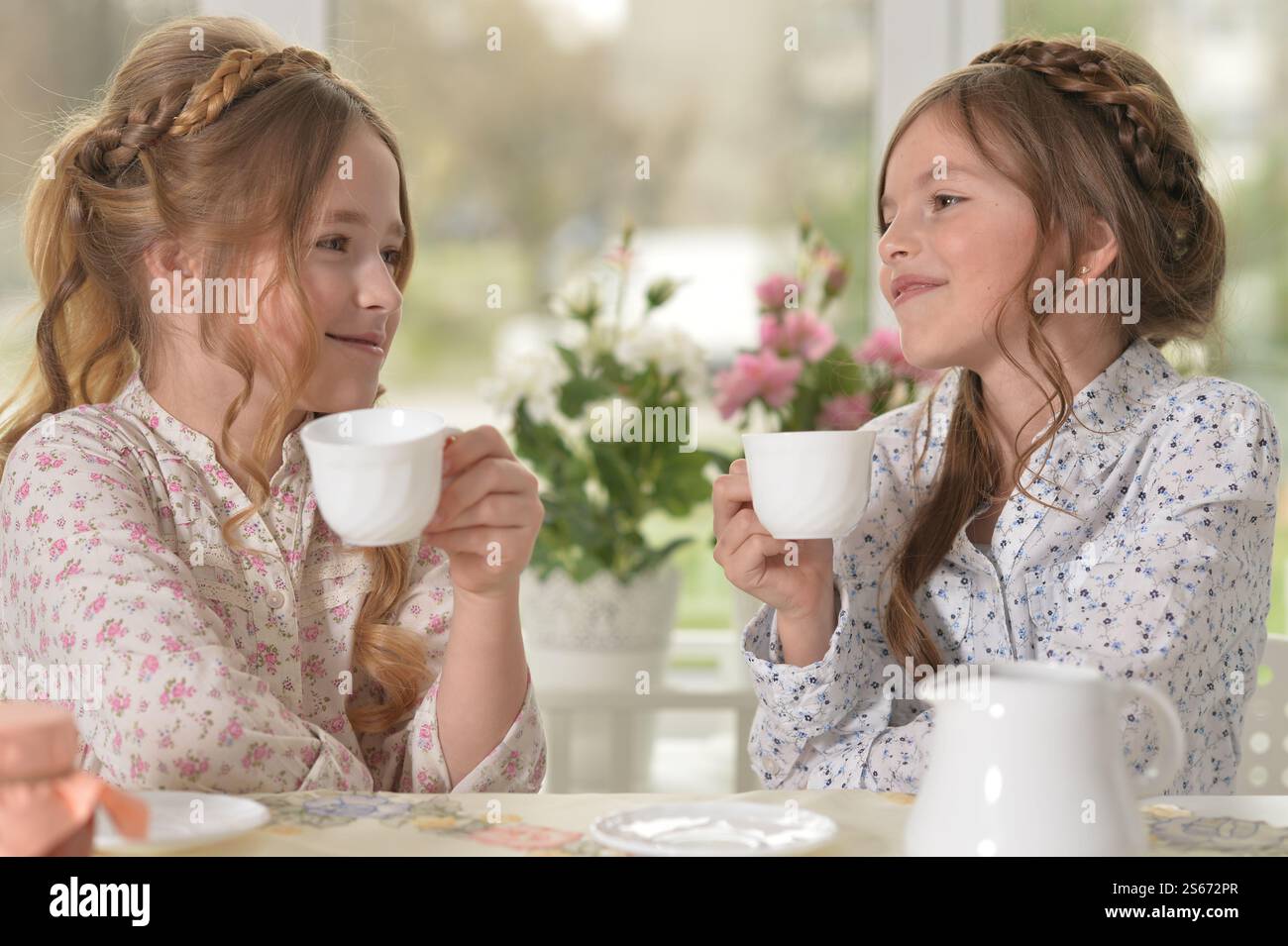 Portrait of two smiling little girls drinking tea at home Stock Photo ...