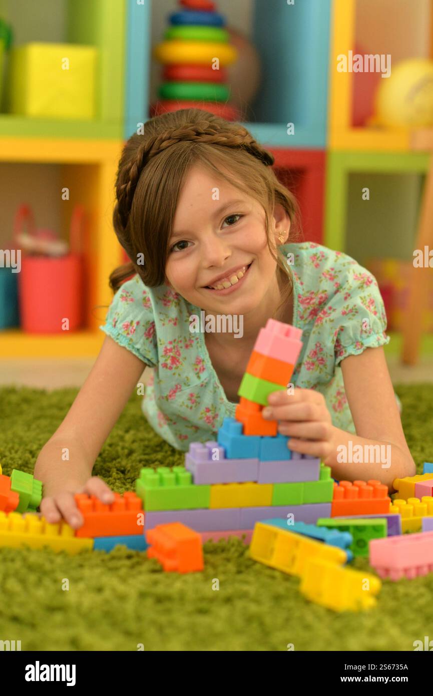 Portrait of cute girl playing with colorful plastic blocks in room ...