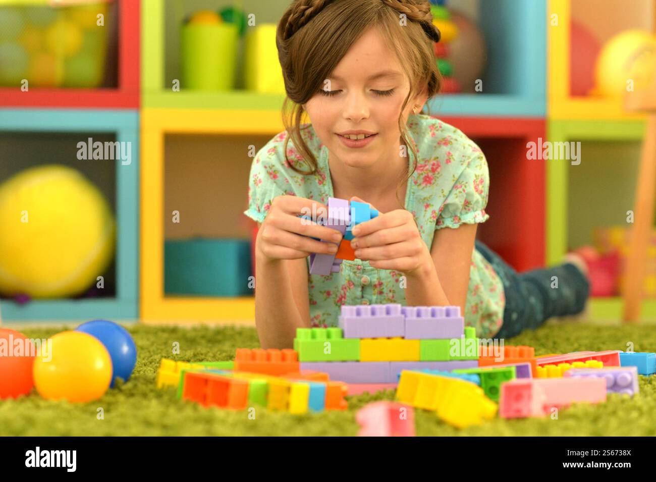Portrait of cute girl playing with colorful plastic blocks in room ...